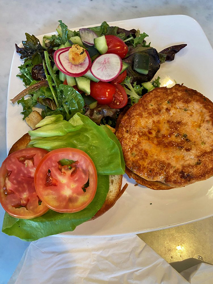 The Spicy Salmon Burger arrives like a California dream—golden-crisp exterior, vibrant salad companions, and a promise of ocean-fresh flavor in every bite.