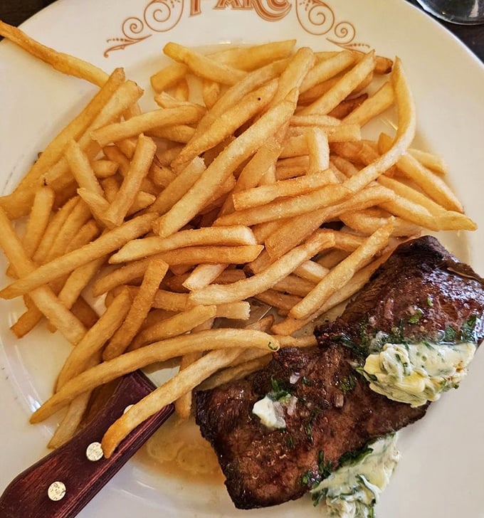 The steak frites arrives like a French declaration of independence from boring meals—crispy fries stacked high beside a perfectly seared New York strip.