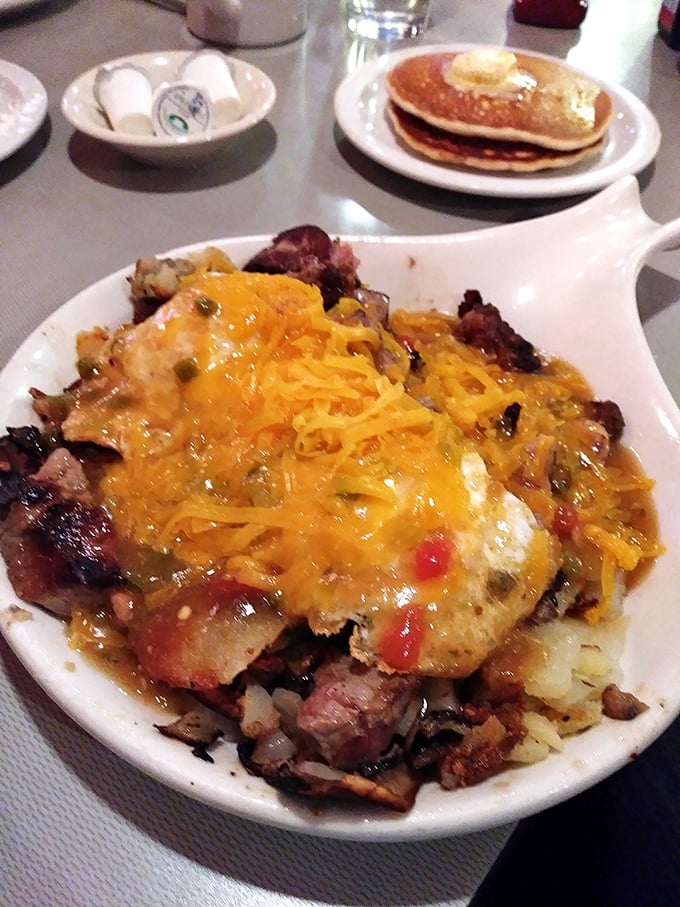 When breakfast goes full Colorado: eggs, potatoes, and meat under an avalanche of green chili. Pancakes standing by for reinforcement.