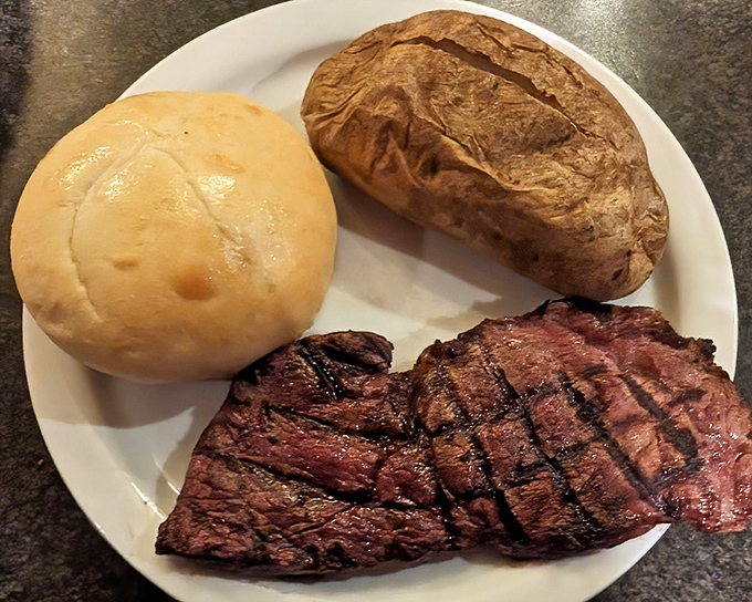 This perfectly grilled steak with a baked potato and roll isn't trying to impress food critics—it's too busy making your taste buds dance with joy.