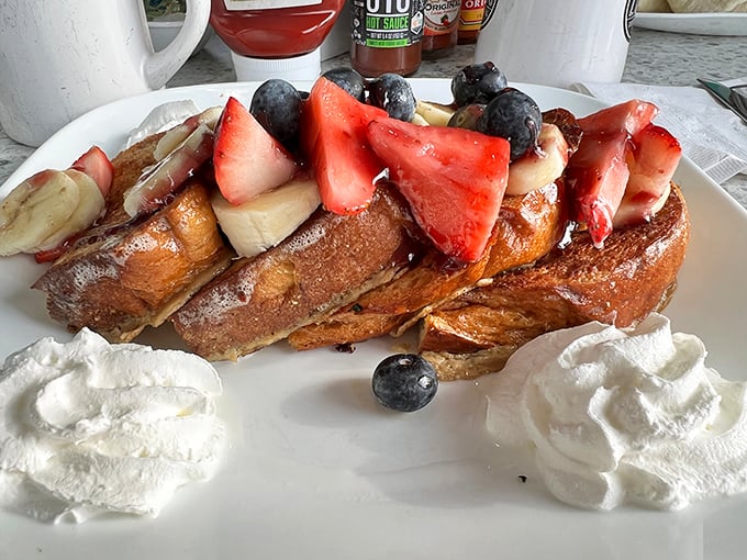 French toast that doesn't just wear fruit—it parades it proudly like edible jewelry, with whipped cream pillows waiting to catch any falling berries.