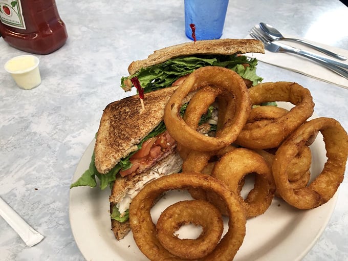 The club sandwich—mankind's greatest architectural achievement involving bread. Those golden onion rings aren't just sides, they're the supporting actors who steal the scene.