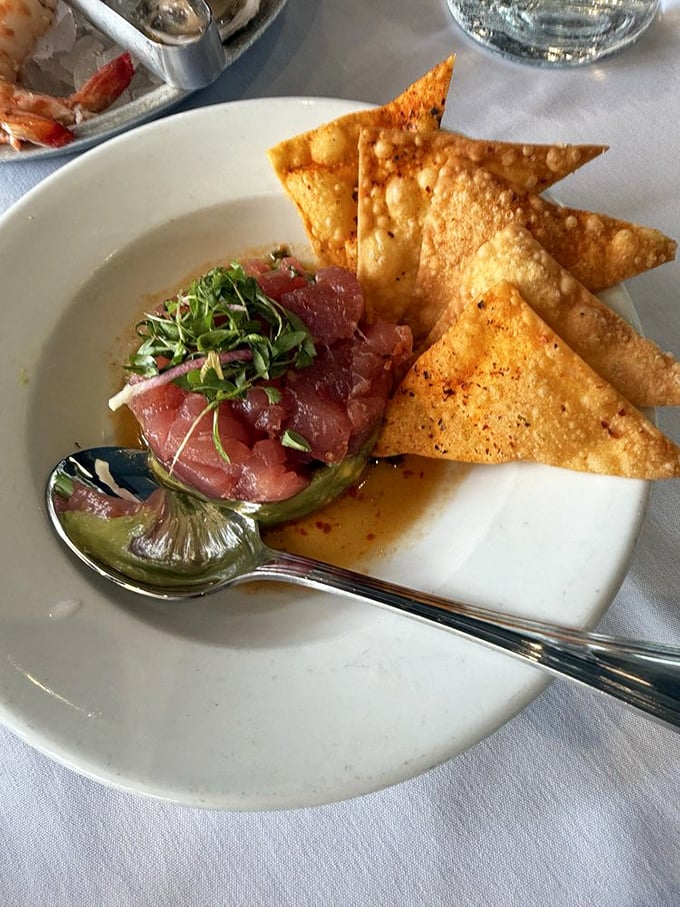The yellowfin tuna poke arrives like jewels from the sea – ruby-red cubes nestled beside crispy wonton triangles, a perfect harmony of textures and flavors.