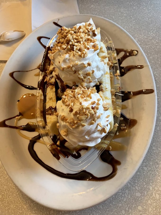 The banana split arrives like dessert royalty on its glass throne—chocolate drizzle and crushed nuts crowning this three-scoop masterpiece.
