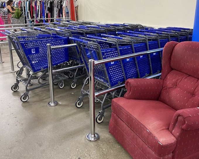 Blue shopping carts stand at attention beside a comfy red recliner—the thrifter's chariot awaits your bargain-hunting expedition.