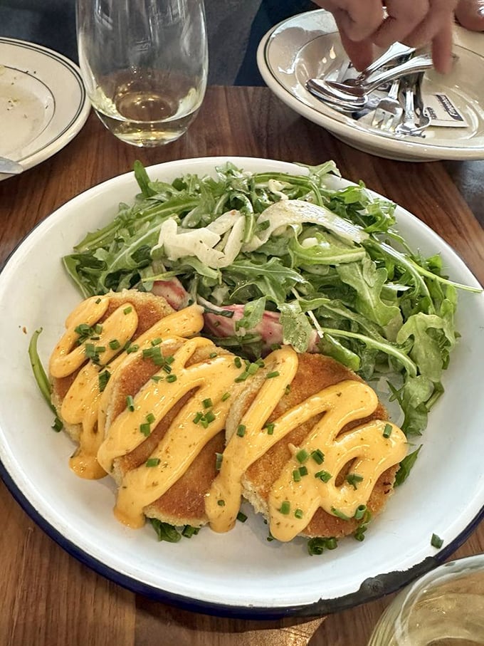 These crab cakes aren't playing around—golden-crisp exteriors giving way to sweet, delicate meat within. The sauce drizzle is just showing off.