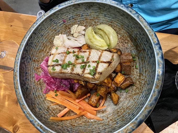 This isn't just grilled swordfish—it's a colorful maritime canvas. The perfectly charred fish rests atop a vibrant medley of roasted vegetables and pickled accents.