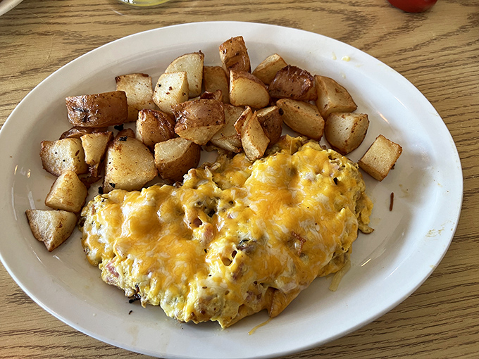 The omelet arrives like a golden sunrise next to perfectly crisped home fries—proof that simplicity, when executed perfectly, needs no embellishment.