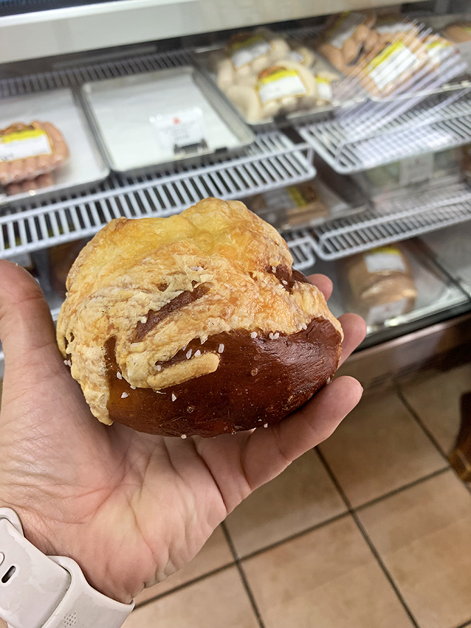 The pretzel roll sits in hand like a small, perfect planet—dense, chewy universe of salt and satisfaction.