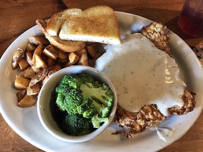 Chicken fried steak drowning in cream gravy with a broccoli sidekick—proof that vegetables can hang with the big boys.