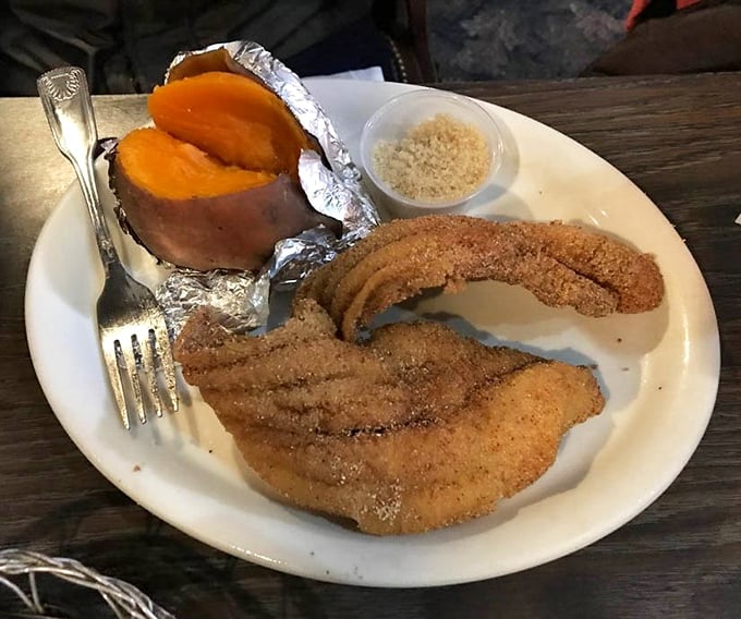 A sweet potato wrapped in foil sits like buried treasure beside perfectly seasoned catfish—comfort food that speaks with a distinct Tennessee accent.