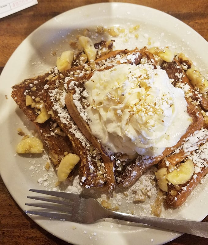 Banana nut French toast crowned with whipped cream and powdered sugar—breakfast that thinks it's dessert, and nobody's complaining.
