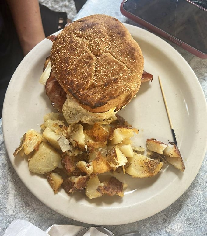 The breakfast sandwich arrives like a morning masterpiece – perfectly toasted bread cradling eggs and bacon with home fries that demand attention.