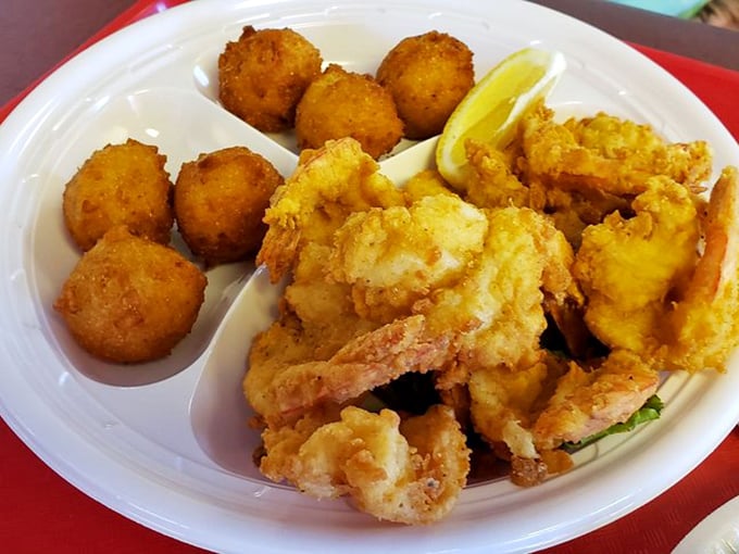 A plate of golden, crispy butterfly shrimp is served with hush puppies and lemon wedges for a delicious seafood meal.