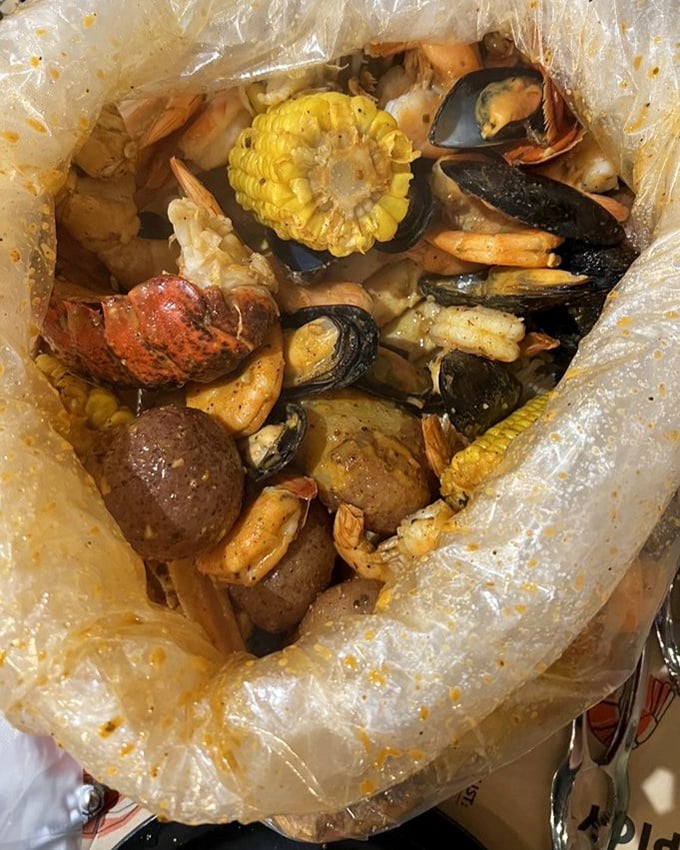 The plastic bag reveals its treasures like a pirate's chest – corn, potatoes, shellfish, and spices mingling in seafood harmony.
