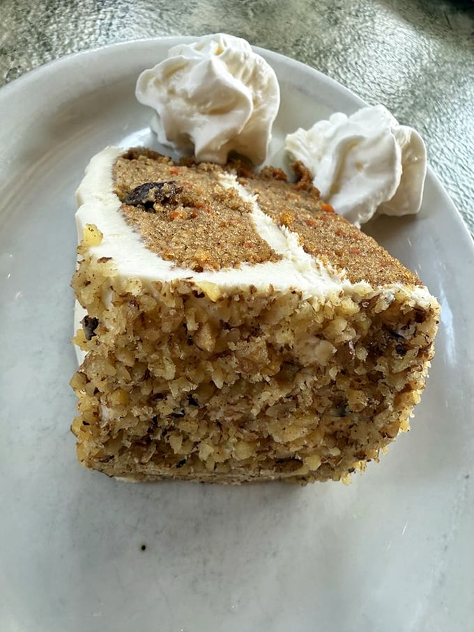 A slice of carrot cake that doesn't skimp on the good stuff—moist, dense, and crowned with cream cheese frosting dollops of pure joy.