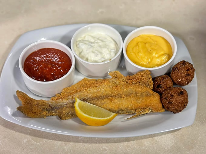 The catfish arrives like a golden ambassador of the South, cornmeal-crusted and flanked by hushpuppies and three dipping sauces—because choices matter.