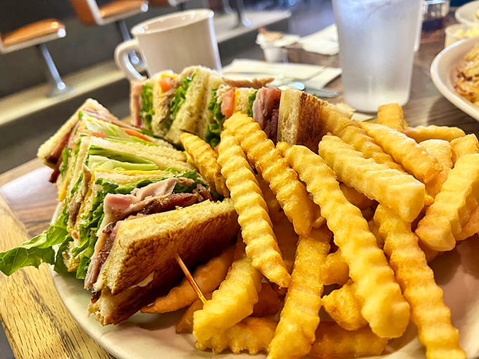 The club sandwich—architecture you can eat. Layers of satisfaction held together by toothpicks and tradition, with a side of crinkle-cut fries that demand to be savored one by one.