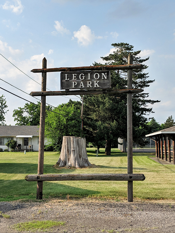 Legion Park's wooden sign frames memories of summer picnics and childhood adventures under ancient trees.