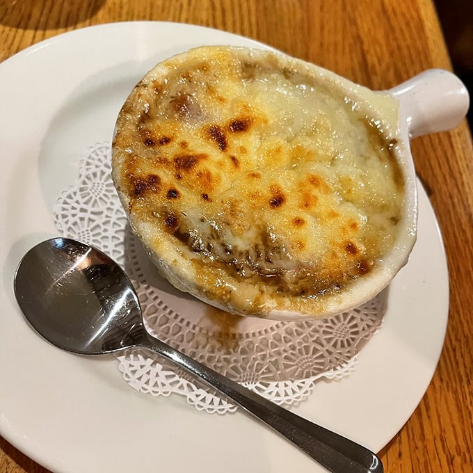 French onion soup done right—a bubbling cauldron of sweet onions beneath a golden cathedral ceiling of melted cheese. Spoon-breaking perfection.