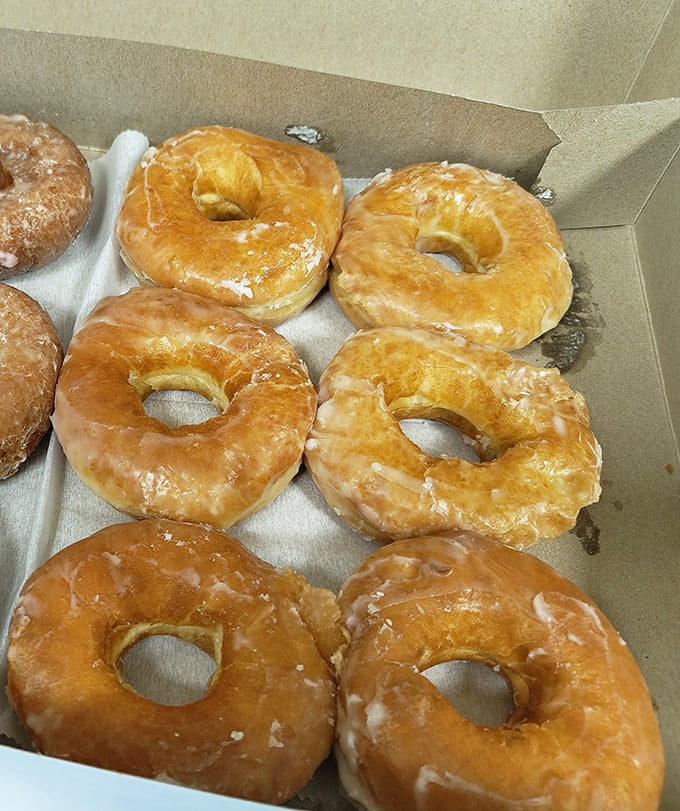 Glazed donuts lined up like soldiers, their shiny armor glistening in the box. Each one perfectly imperfect, a testament to human hands at work.