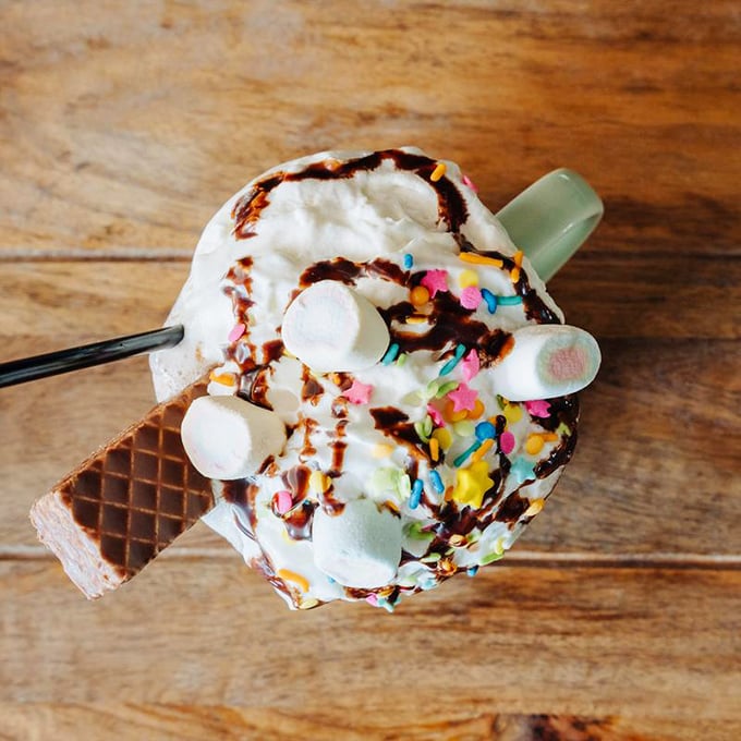 Hot chocolate elevated to an art form—topped with whipped cream, marshmallows, and sprinkles that would make Willy Wonka nod in approval.