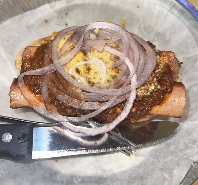 A hot dog elevated to art form, topped with savory chili and fresh onions—proof that simple pleasures done right can be the most satisfying.