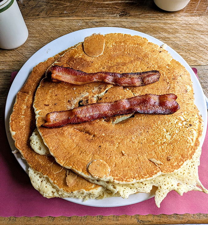 Pancakes so magnificent they deserve their own ZIP code. Those bacon strips aren't garnish—they're the VIP guests at this carb carnival.