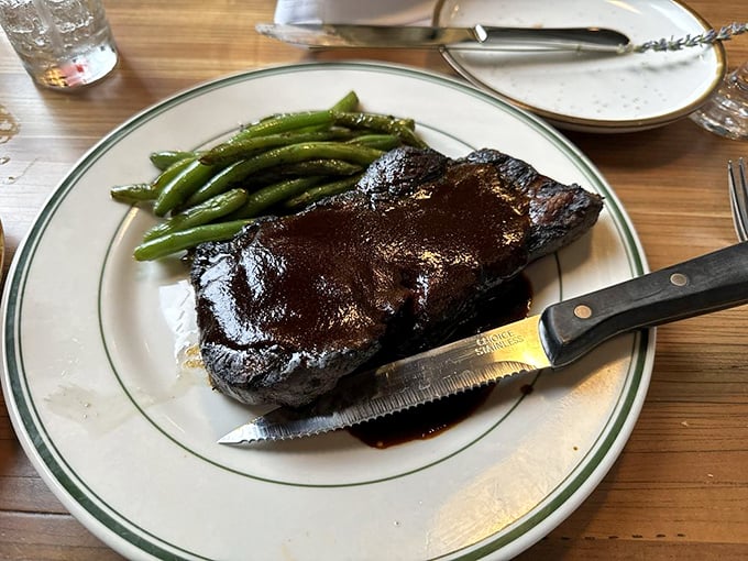 A New York strip steak glistening with promise, flanked by vibrant green beans—proof that sometimes the simplest preparations yield the most profound satisfaction.