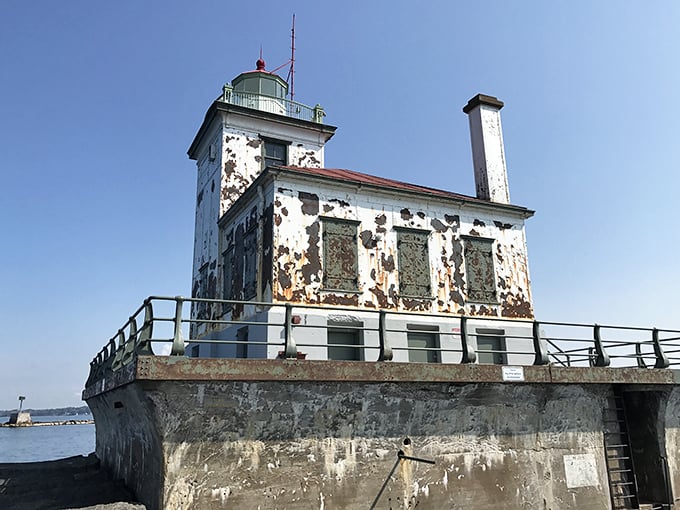 The weathered Oswego West Pierhead Lighthouse stands sentinel at the harbor entrance, wearing its age with the dignity of a silver-haired sea captain.