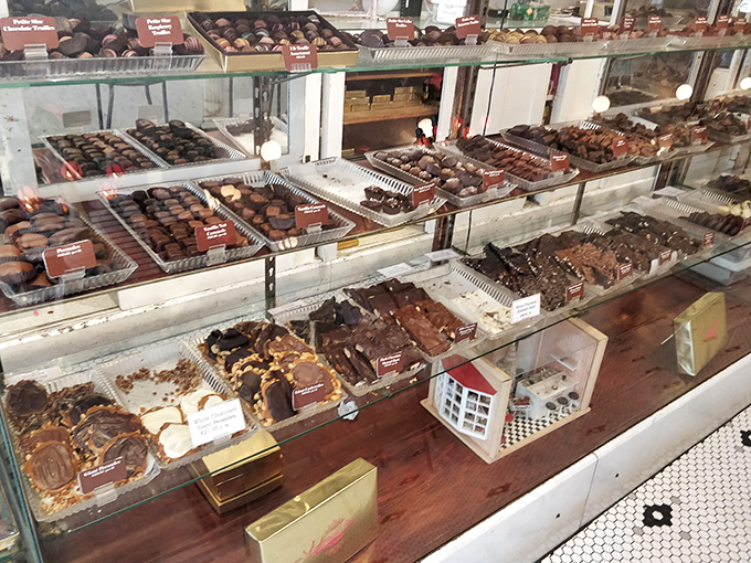 The chocolate display case—where adults press their noses against glass like children. Each handcrafted piece arranged with the precision of museum artifacts.