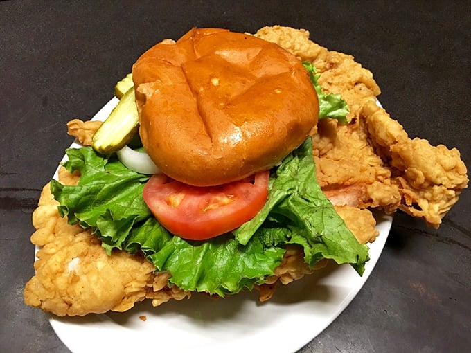 This pork tenderloin sandwich has clearly never heard of plate boundaries—the crispy, golden-fried masterpiece refuses to be contained by mere bread.