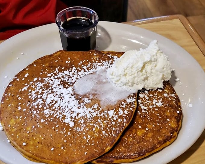 Golden pumpkin pancakes dusted with powdered sugar and topped with real whipped cream—breakfast that feels like dessert but somehow counts as a legitimate meal.