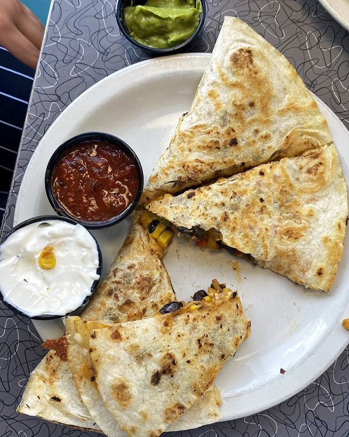 The quesadilla arrives golden and crisp, oozing with melted cheese and stuffed with savory fillings—comfort food that crosses cultural boundaries with delicious results.