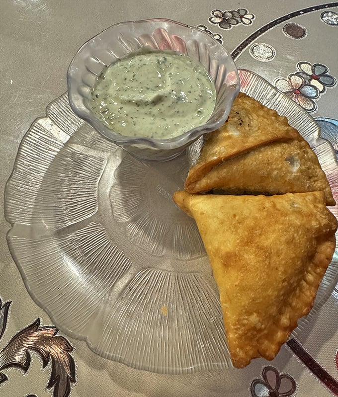 Golden samosas beside cooling raita—the perfect fried triangle that makes "just one more" an absolute impossibility.