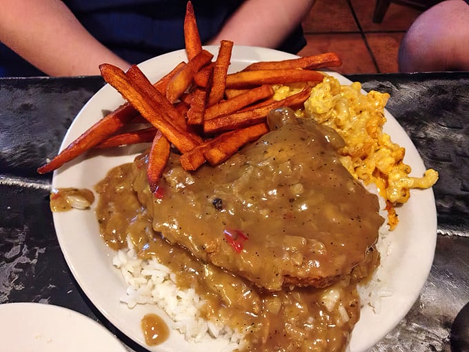 Smothered pork chop swimming in rich gravy alongside sweet potato fries and mac & cheese – a holy trinity of comfort food.