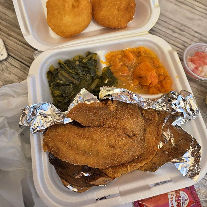 This fried fish with greens and sweet potatoes isn't just a meal—it's a Southern symphony on a styrofoam stage.