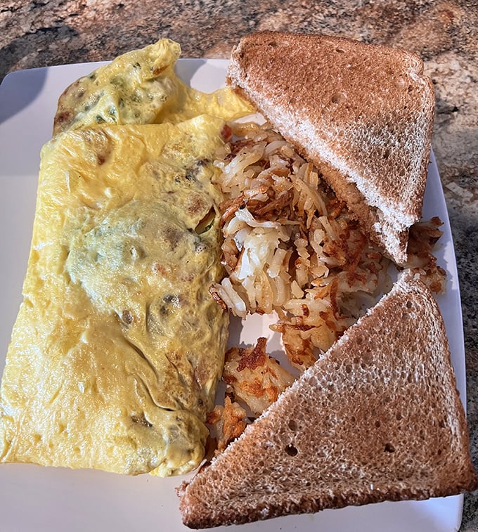 Breakfast alchemy at its finest—a fluffy omelet alongside crispy home fries and toast. The morning trifecta that never disappoints.