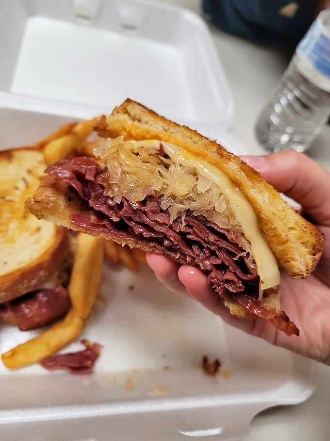 The Reuben sandwich in mid-bite glory—where corned beef, sauerkraut, and Swiss cheese perform a perfect harmony of flavors.