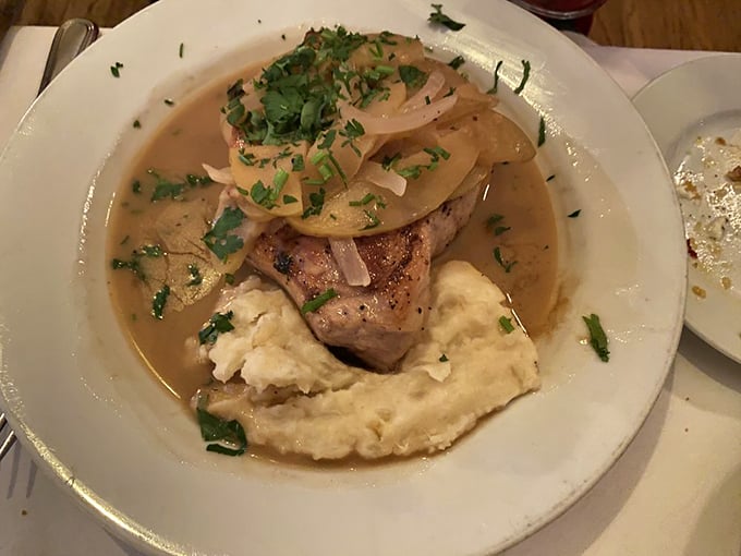 This pork chop doesn't just sit on mashed potatoes—it reigns over them, crowned with caramelized onions in a sauce worth sipping like fine wine.