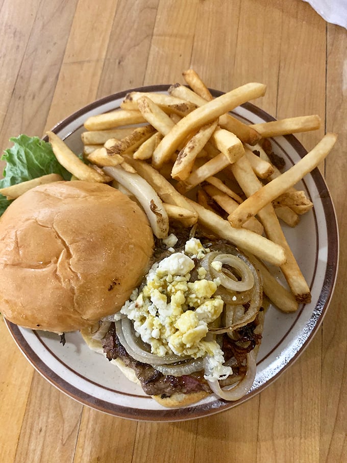 The burger arrives like a savory sonnet—hand-formed patty, grilled onions, and blue cheese crumbles creating a flavor poem that makes fast food chains weep with inadequacy.