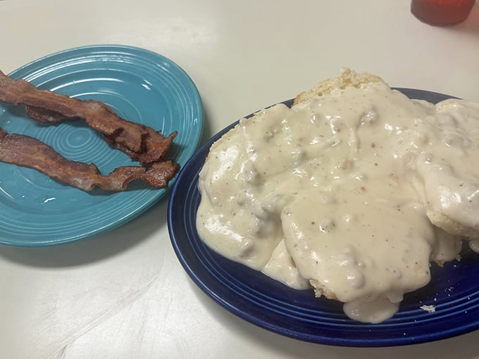 Biscuits swimming in peppery gravy alongside perfectly crisp bacon strips—proof that sometimes the simplest combinations create the most profound happiness.