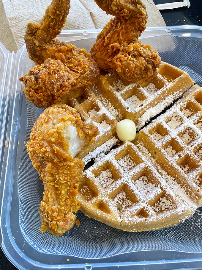 The holy grail—crispy golden chicken perched atop a powdered waffle with a pat of butter melting into those perfect squares.