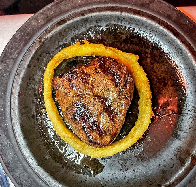 A filet mignon surrounded by a golden onion ring crown—proof that sometimes the simplest presentations deliver the most profound flavors.