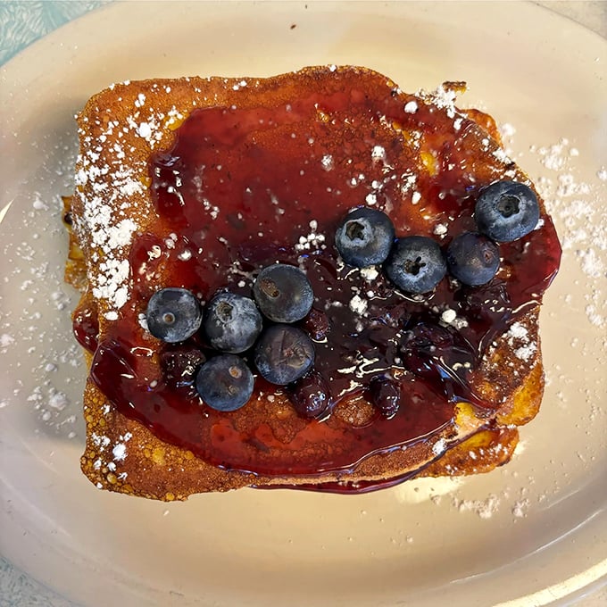 French toast that dreams are made of – golden, crispy edges giving way to custardy centers, crowned with fresh blueberries and a dusting of powdered sugar.