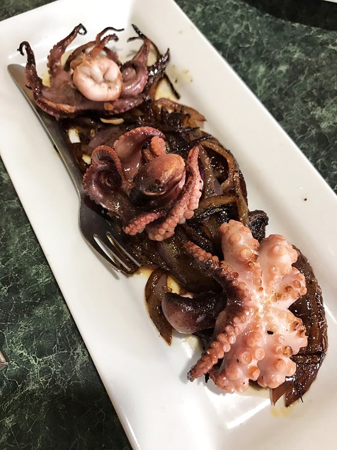 Charred baby octopus with grilled onions—tender, smoky, and proof that eight legs can be absolutely delicious on your fork.