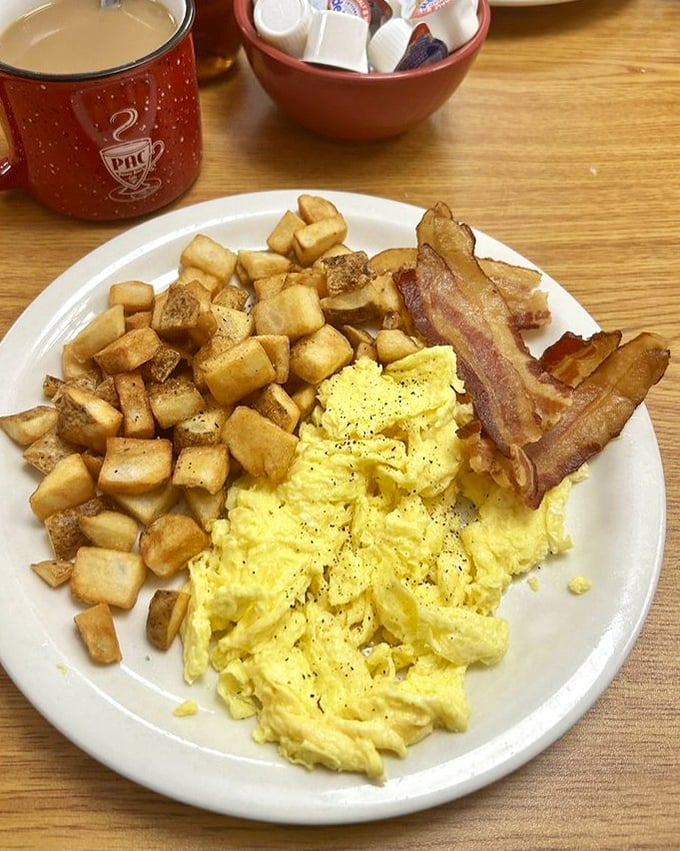 The breakfast trinity: fluffy eggs, crispy potatoes, and bacon that snaps like nature intended. Simple perfection on a white plate.