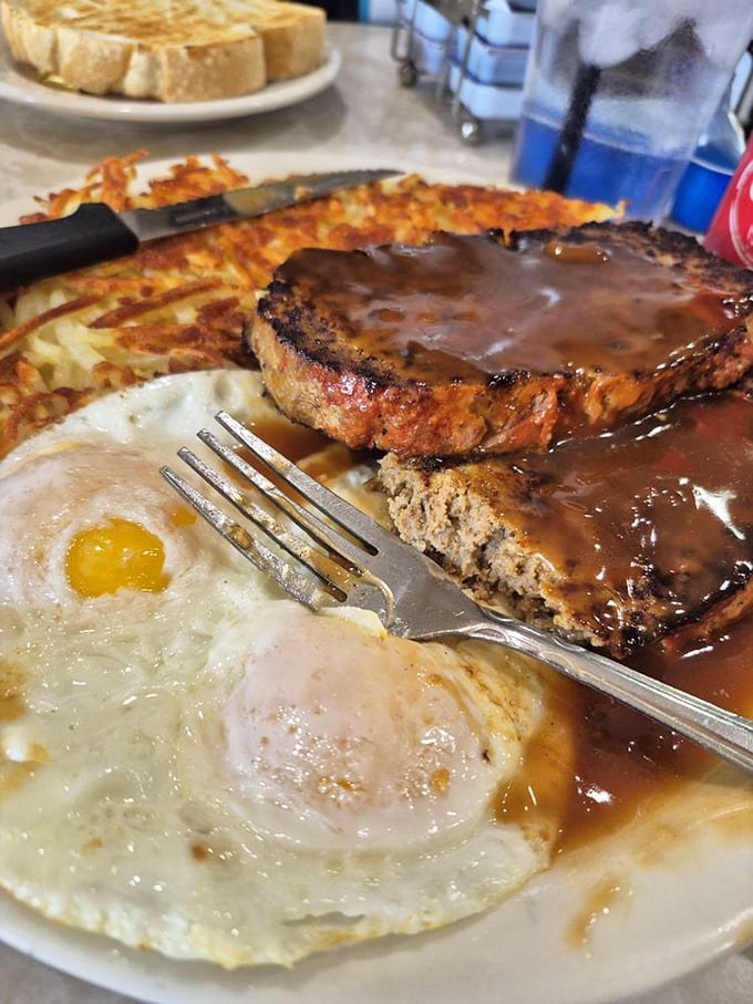 The breakfast of champions: eggs sunny-side up, crispy hash browns, and meatloaf smothered in gravy – a plate that says "go back to bed" and "conquer the world" simultaneously.