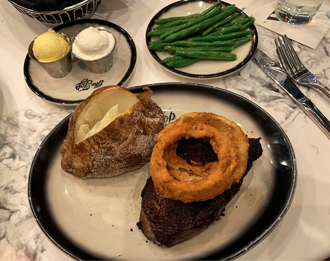 A steak with an onion ring crown—because even royalty needs the perfect accessory. The baked potato stands ready for its supporting role.