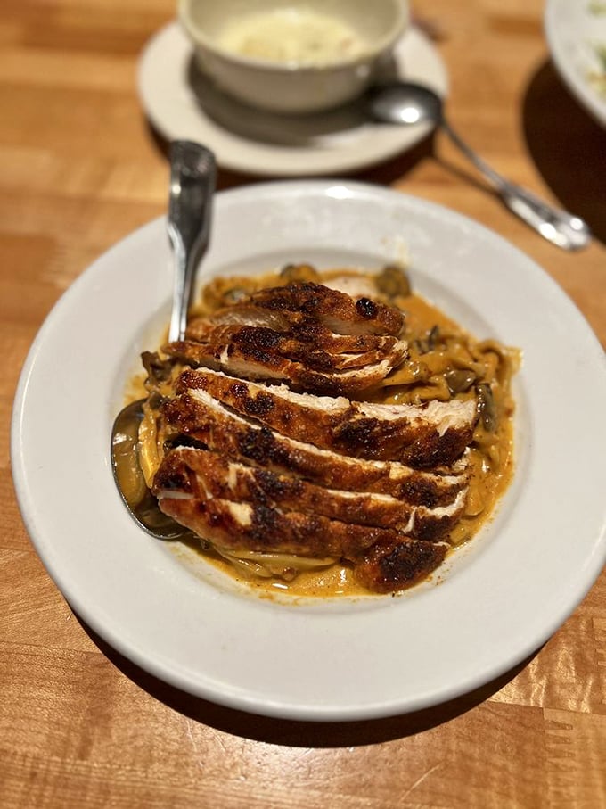 Blackened chicken rests atop a bed of pasta like a perfectly seasoned crown, surrounded by a sauce that's clearly been simmering with purpose and intention.